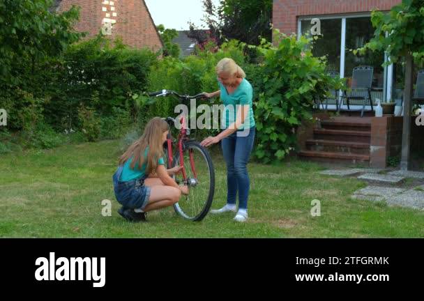 Mom Helps Her Daughter Fix Her Bicycle In The Backyard Of The House