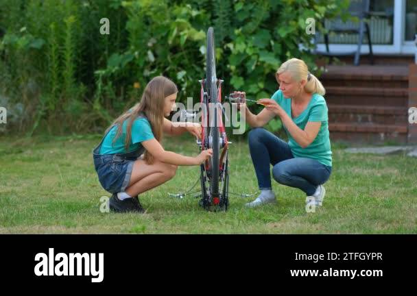 Mom Helps Her Daughter Fix Her Bicycle In The Backyard Of The House