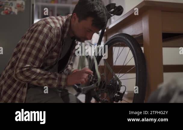 Man is fixing bicycle at home. Male repairs his bike at home. Guy is ...