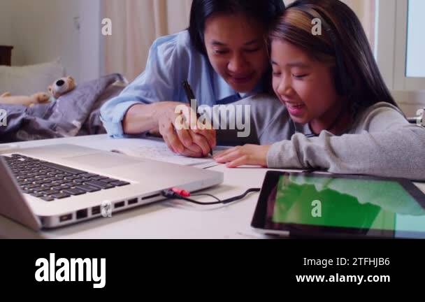 4K Asian young little girl using laptop to study with her mother. Student kid writing homework ...