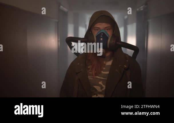 Woman in grunge clothes hooded mantle and gas mask standing in dark ...