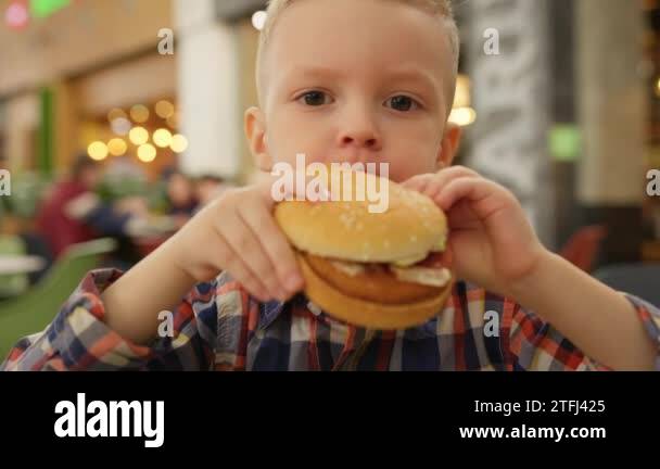 Blond caucasian 4-year-old boy eats hamburger with beef in fast food ...