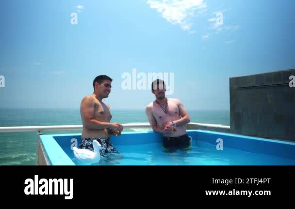 two friends toasting with whiskey inside a pool on a terrace with a ...