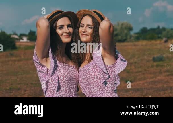 Portrait of two smiling young twin women in summer dresses and straw ...