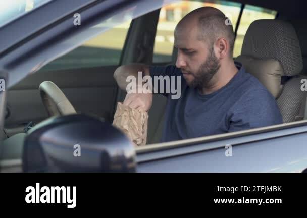 Serious man eating fast food while driving a car. The taxi driver ...