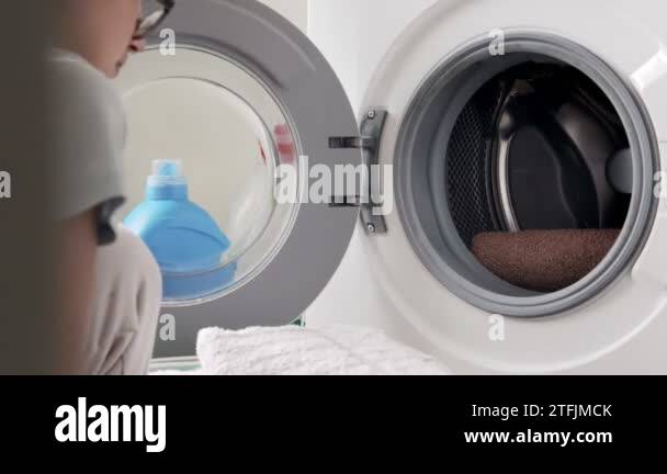 Woman puts a capsule of washing powder in the washing machine. Loading ...
