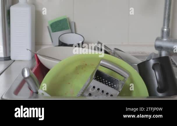 The kitchen utensils in the wash basin need to be washed. A pile of ...