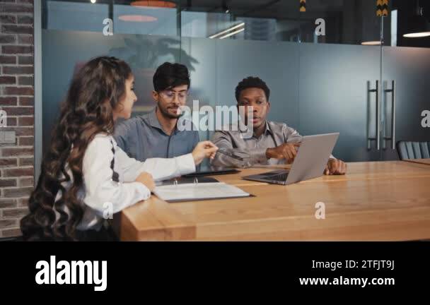 Multiracial colleagues sit in office at table discuss project ideas ...
