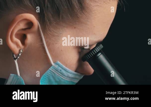 Girl Scientist Looks Into the Lens of a Microscope in a Mask Close-up ...