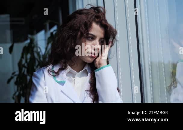 Close up view of sad tired woman doctor with curly hair looking through ...