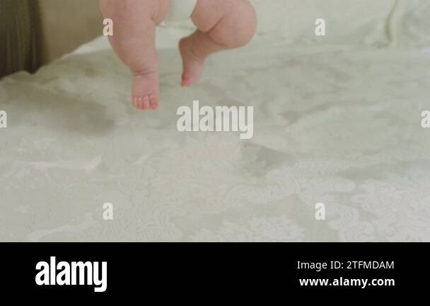 Cute baby are jumping over the bed while the mother are holding the ...