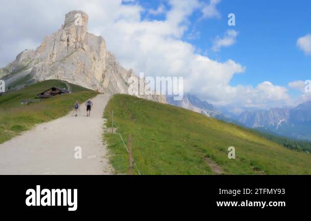 Couple of hikers walk on a sand and stone pathway in high mountain that ...
