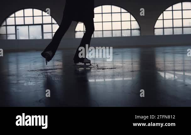 Young woman is skating on dark ice arena. Close up of female legs in ...