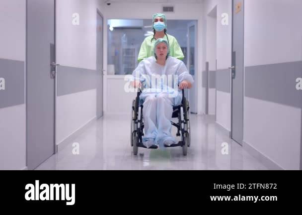 Dolly shot teenage girl in wheelchair with nurse pushing mobility aid ...