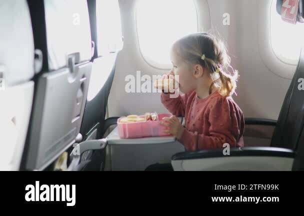 4 year old girl eating snacks from lunch box while travelling by plane ...