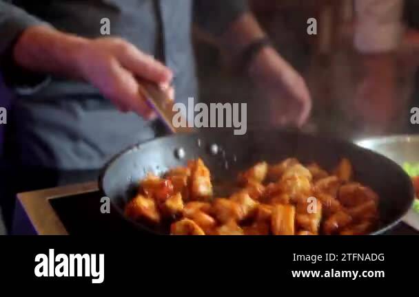 Chef is tossing crispy chicken pieces while cooking it with spicy sauce ...