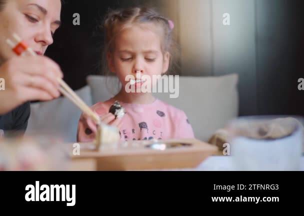 Child eat sashimi in restaurant. Middle shoot little girl with mother ...