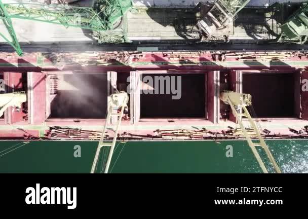 Loading dry cargo ship of wheat by cranes in port. Top down view loading into holds of sea cargo ...