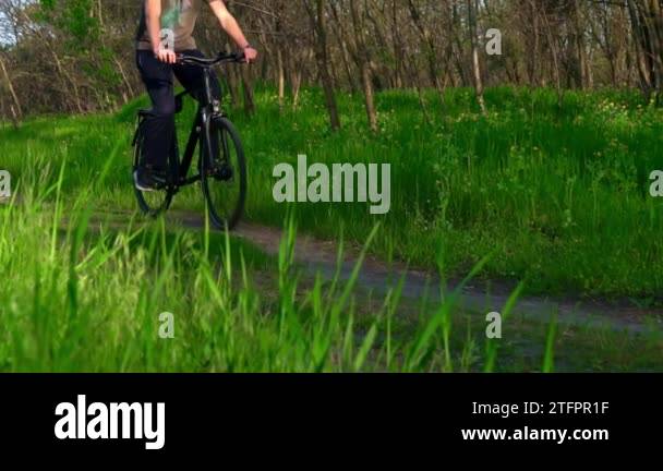 Young guy rides a bicycle along a dusty path in the forest at sunset. A ...