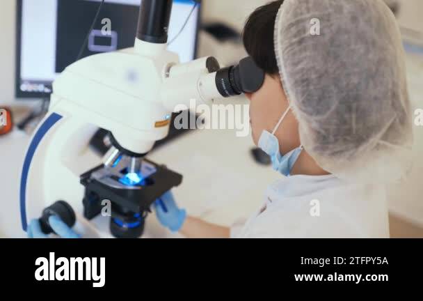 a doctor in a modern clinic works behind a fluorescent led microscope ...