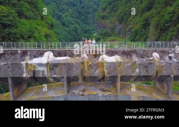 Company of four people walk across large concrete pedestrian bridge ...
