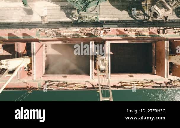 Loading dry cargo ship of wheat by cranes in port. Top down view loading into holds of sea cargo ...