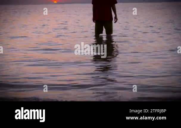 Tilt up to man standing in water in worship pose reaching out towards ...