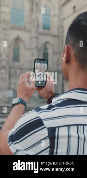 VERTICAL VIDEO: Young man tourist taking photo of sights. Back view ...