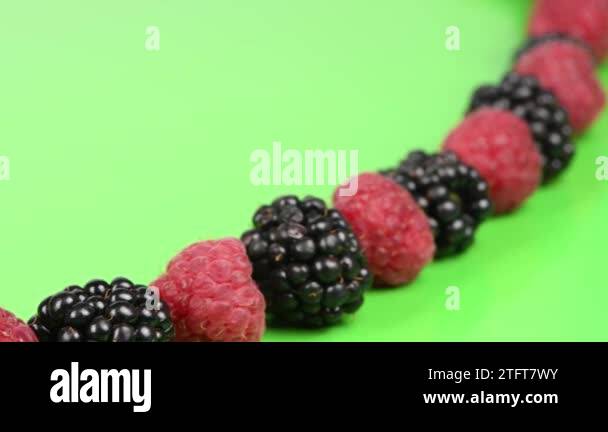 Raspberries alternate with blackberries on green background. Movement ...