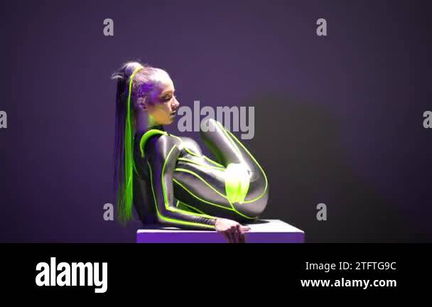Young slim woman sitting on cube in strobe lights looking at camera ...