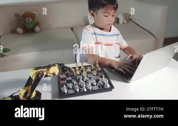 Asian little boy programming code to robot machine arm on laptop for ...