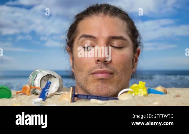 A man buried up to his head on a beach filling up with trash and ...