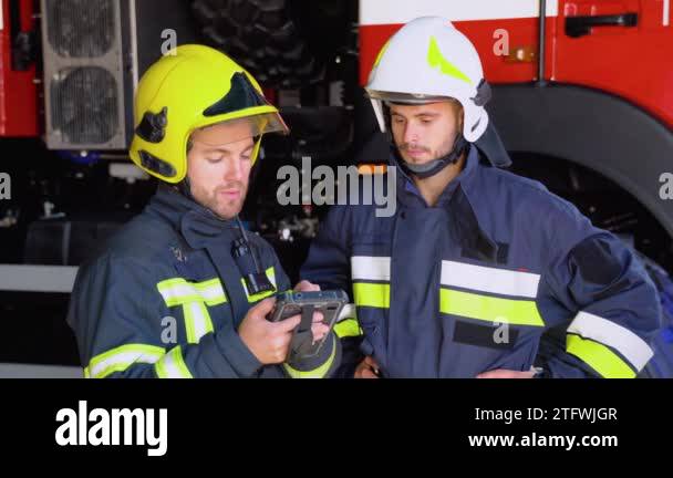 Two firemen in full equipped clothes standing outside at the fire truck ...