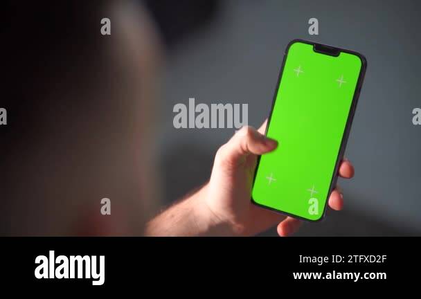 The man is using his phone in a vertical position. The green screen of the smartphone for chroma ...