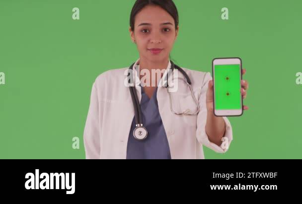 Hispanic woman doctor holding phone with green screen up to camera for ...