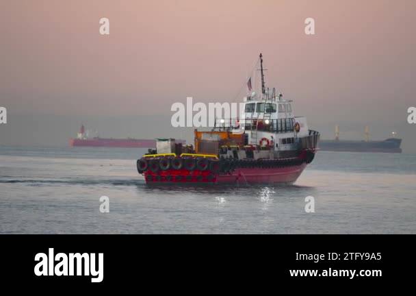 A tugboat turns out to sea with container ships in the background ...