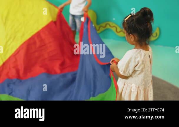 Little dark-skinned girl in dress holding one corner of rainbow play ...