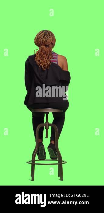 Vertical video: Back view of girl on chair sitting in greenscreen ...