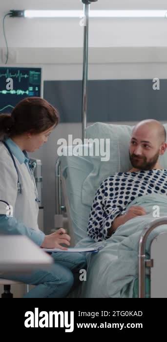 Vertical video: Black nurse checking patient vitals monitoring heart rate injecting vitamin in ...