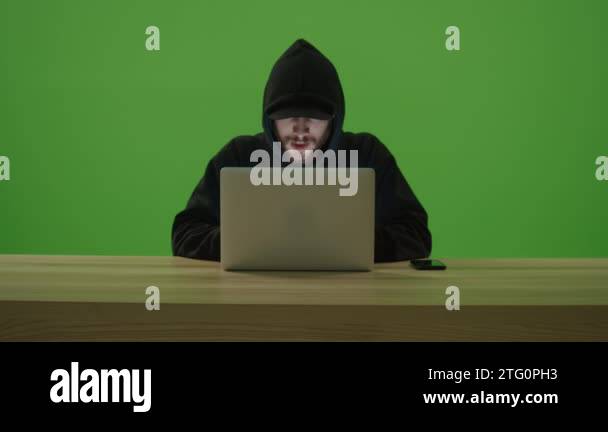 Unrecognizable Man Hacker Wearing Sweatshirt With Hood And Cap Typing On Laptop Computer