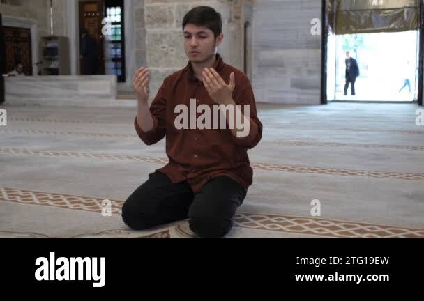 Muslim young man praying with raising hands inside mosque, view of ...