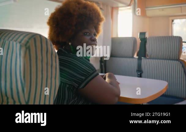 Young adult black woman with afro sitting by table in camper van ...
