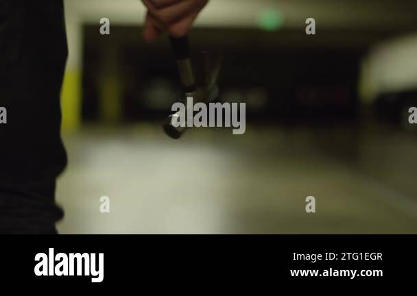 A man quickly aggressively walks through a car parking with a hammer in ...