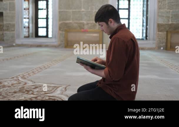 The image of a young man reading the Quran while sitting on his knees ...