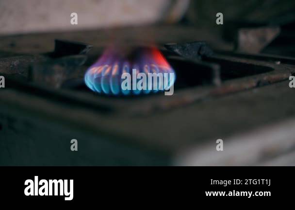 Blue fuel burns in the burner of an old untidy kitchen stove close-up ...