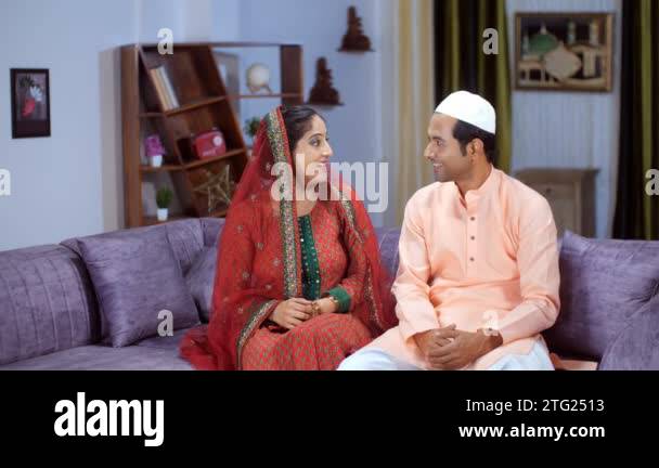 A happy Muslim couple sitting and talking together in their living room ...