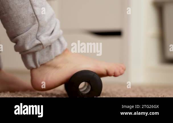 Woman doing flatfoot correction gymnastic exercise using massage roller ...