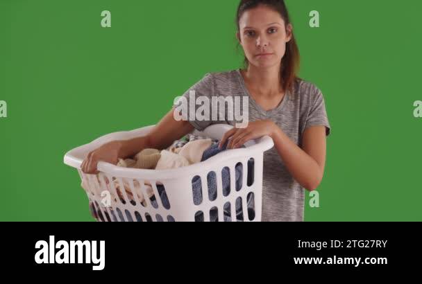 Serious young woman carrying laundry basket of dirty clothes on green ...