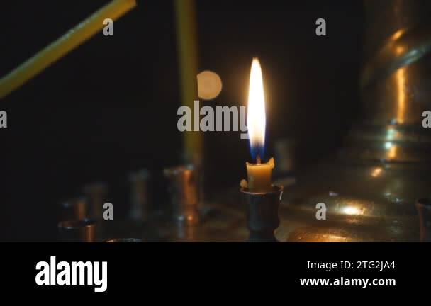Lighting wax candles inserted in sand burning in temple spreading light ...