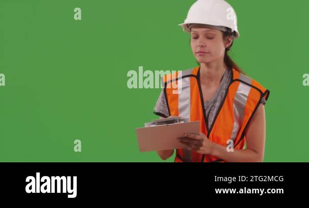 Female construction worker writing notes on clipboard on green screen ...